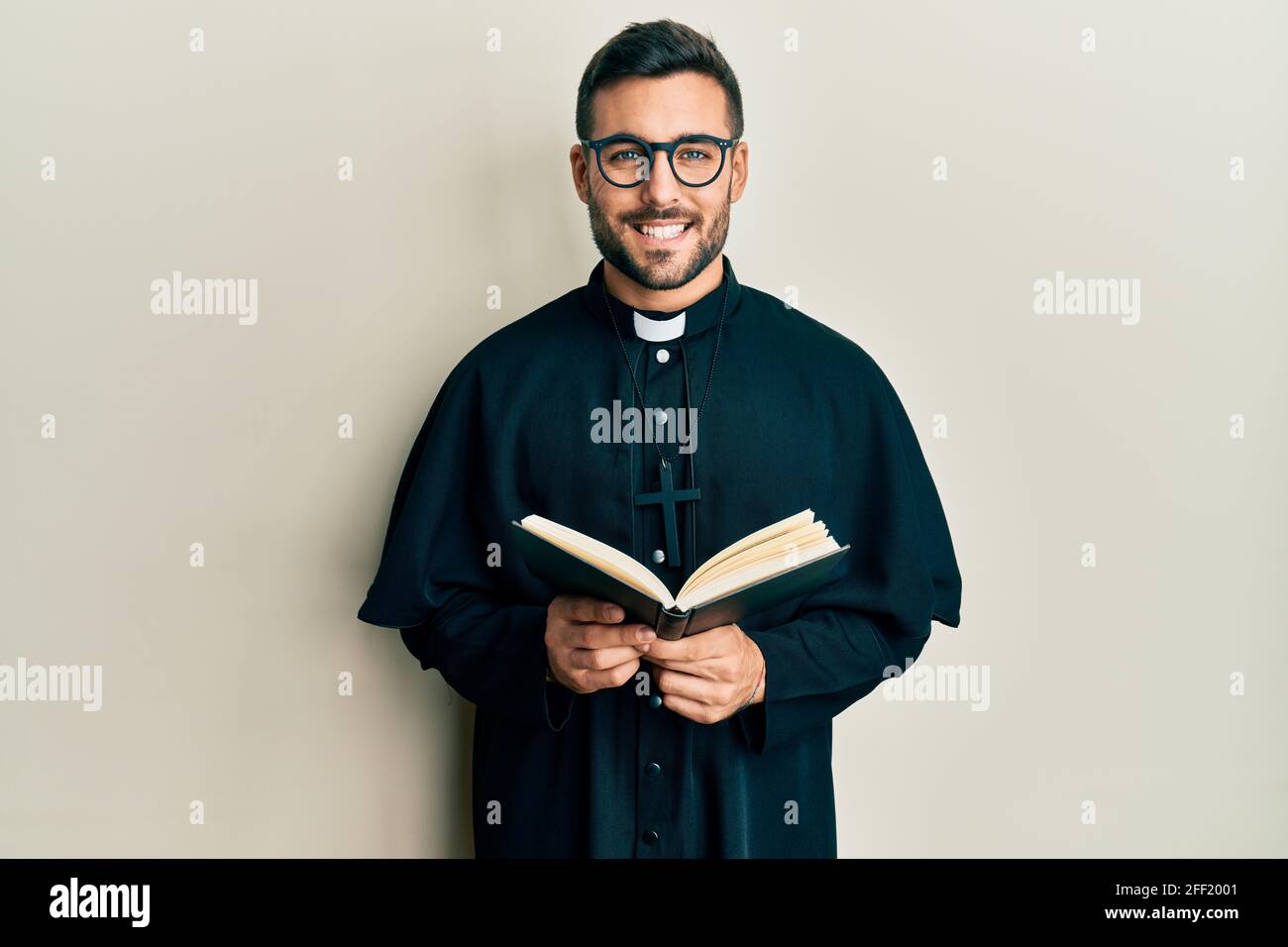 Young hispanic priest man holding bible smiling with a happy and cool ...