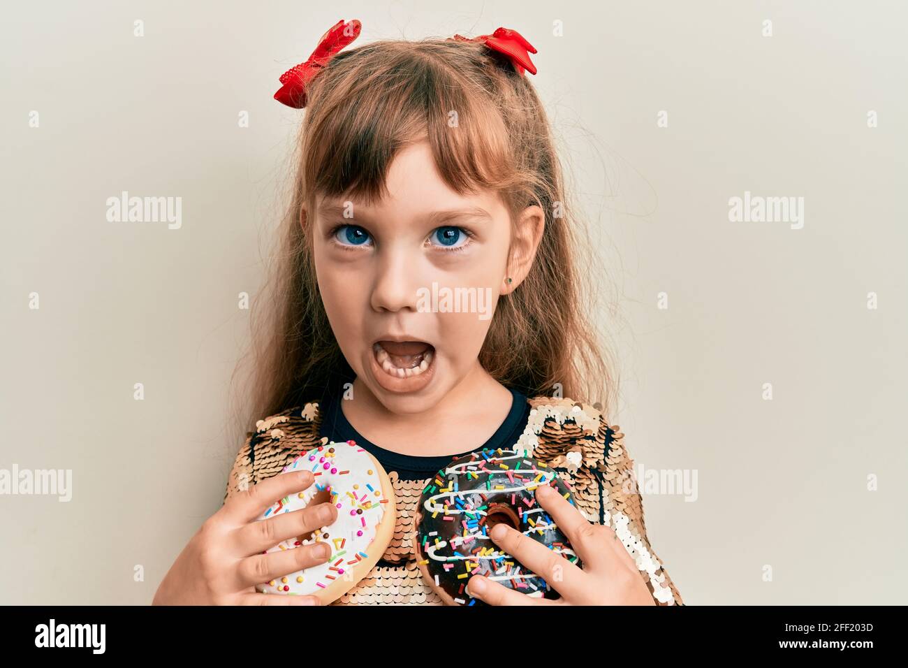 Little caucasian girl kid holding tasty colorful doughnuts clueless and ...
