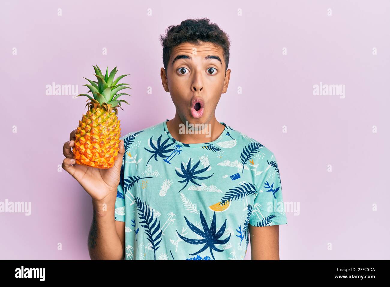 Young handsome african american man holding pineapple scared and amazed ...