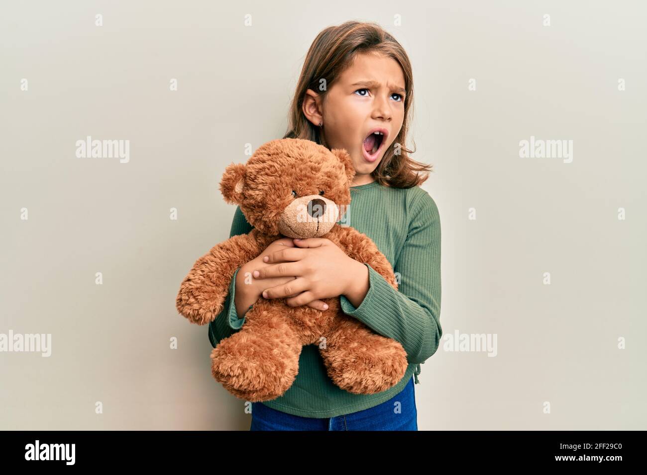 Little beautiful girl hugging teddy bear angry and mad screaming ...