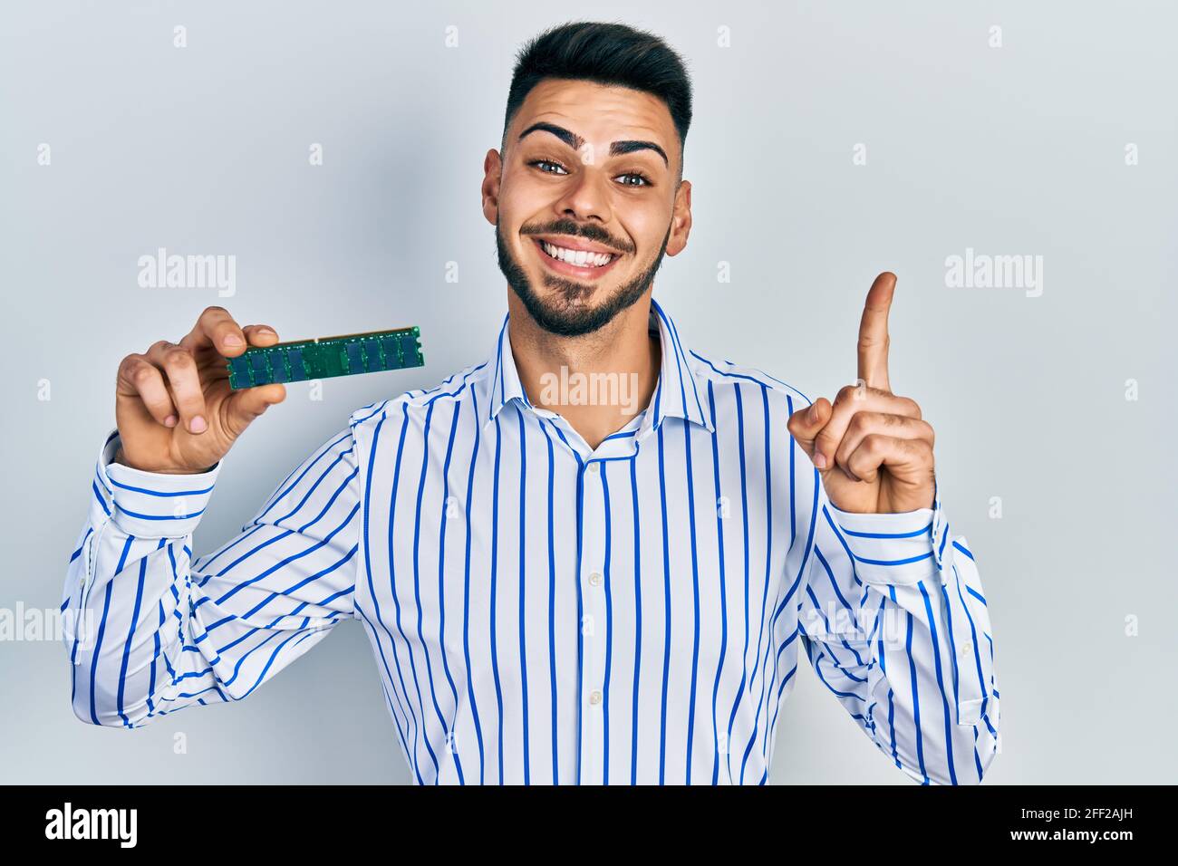 Young hispanic man with beard holding memory ram smiling with an idea ...