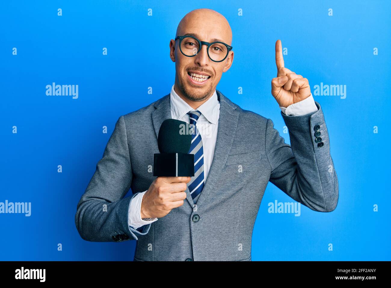 Bald man with beard holding reporter microphone smiling with an idea or ...
