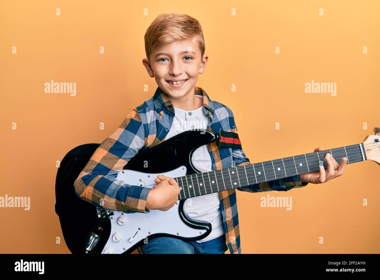 Little caucasian boy kid playing electric guitar smiling with a happy ...