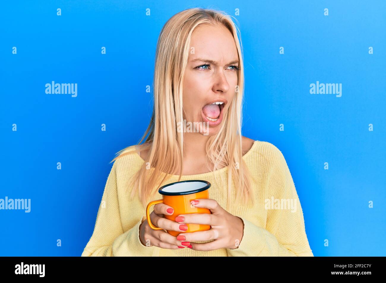 Young blonde girl holding coffee angry and mad screaming frustrated and ...