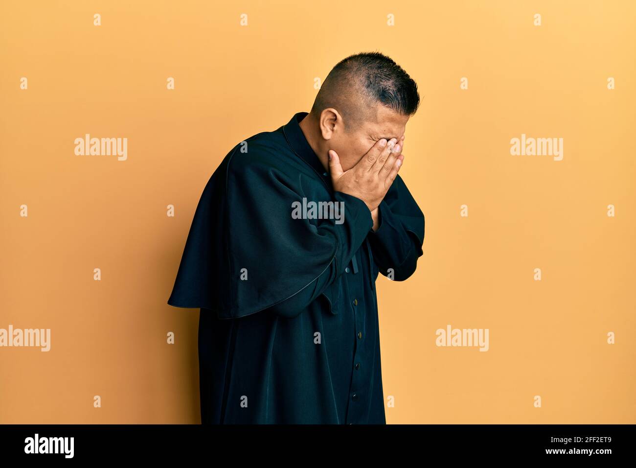 Young latin priest man standing over yellow background with sad ...