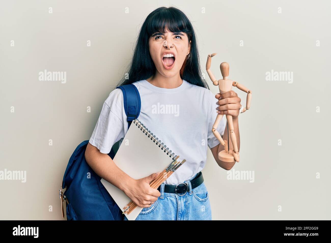 Young hispanic art student girl holding wooden manikin and notebook ...