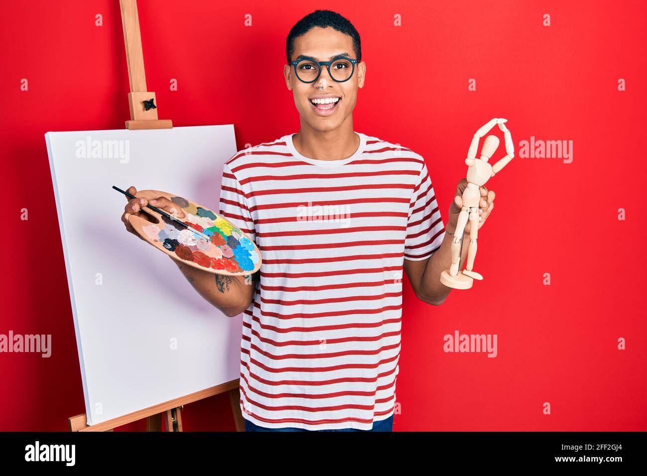 Young african american guy holding painter palette and art manikin ...
