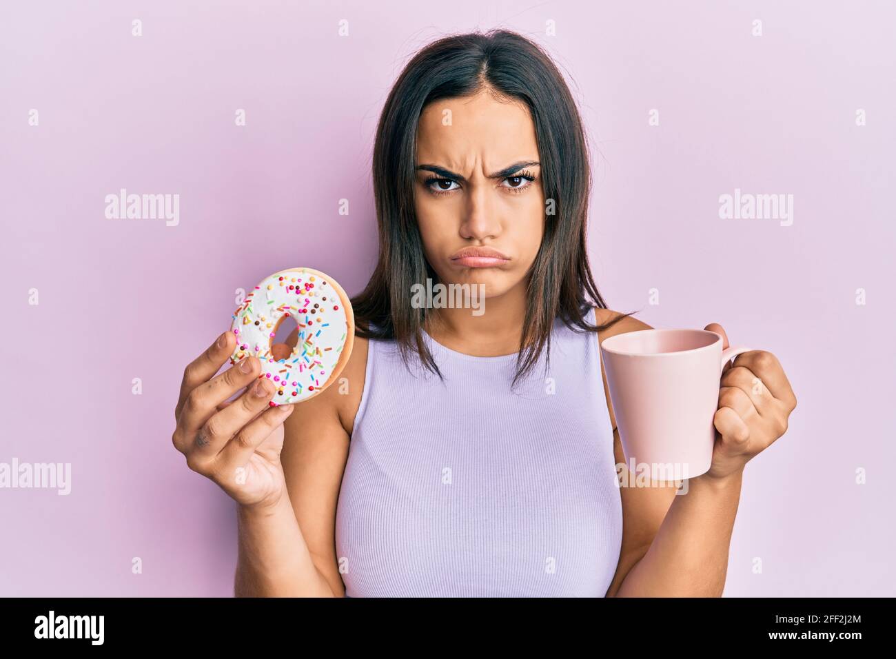 Young brunette woman eating doughnut and drinking coffee depressed and ...