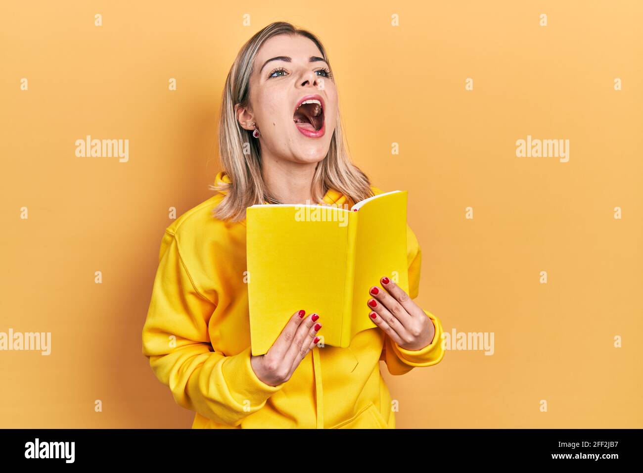 Beautiful caucasian woman holding open book angry and mad screaming ...