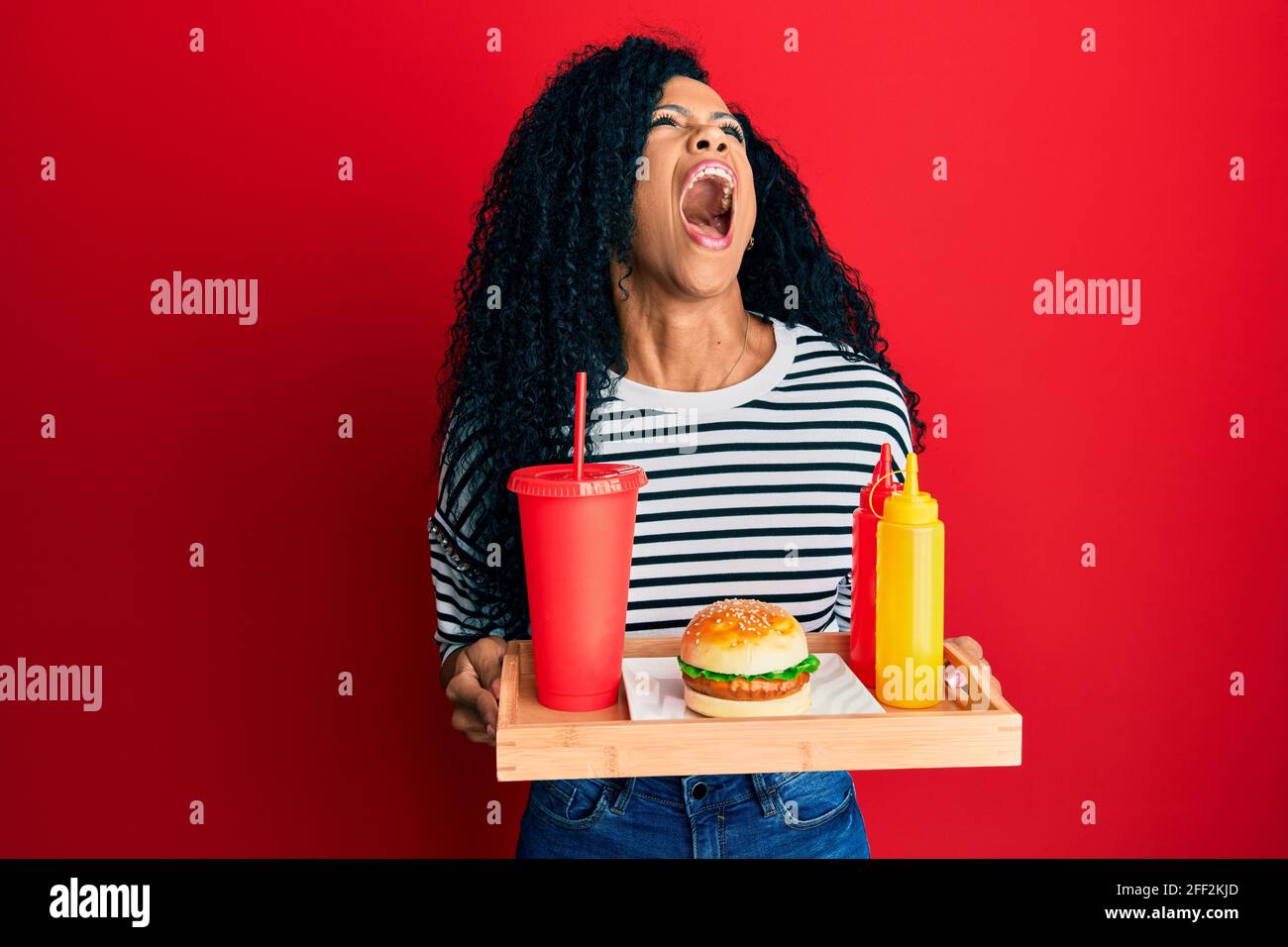 Middle age african american woman eating a tasty classic burger angry ...