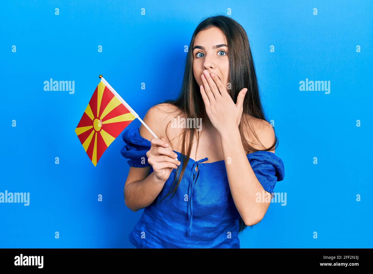 Young brunette teenager holding macedonian flag covering mouth with ...