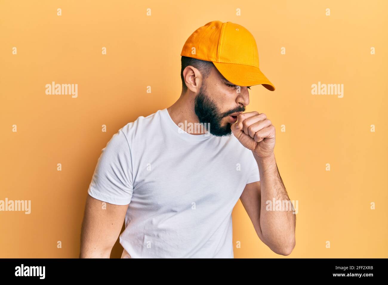 Young man with beard wearing yellow cap feeling unwell and coughing as ...