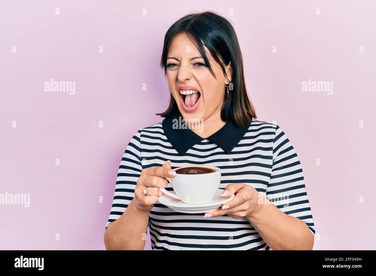 Young hispanic woman drinking a cup of coffee angry and mad screaming ...