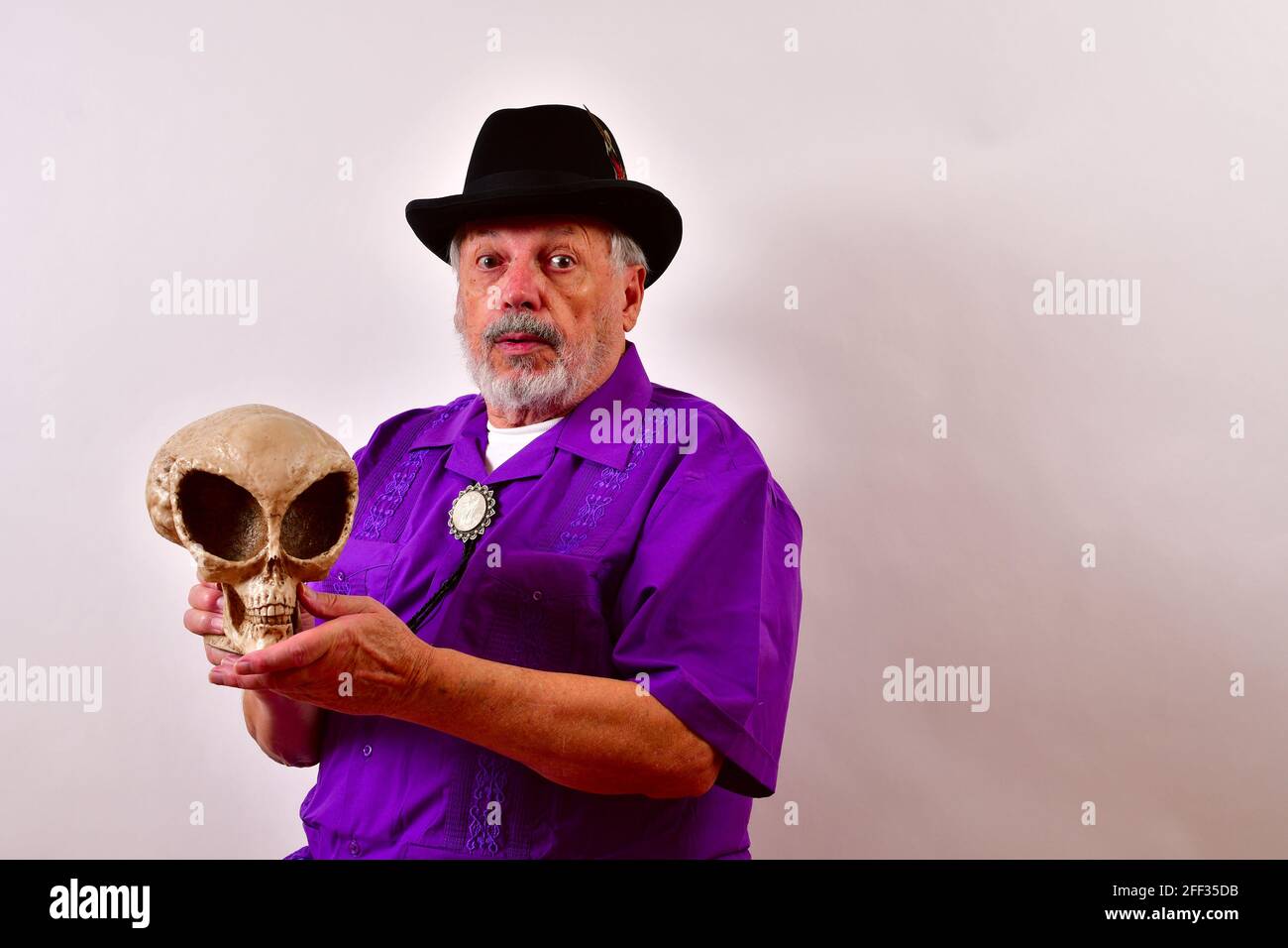View of an elderly man with a purple shirt and a hat holding his alien ...