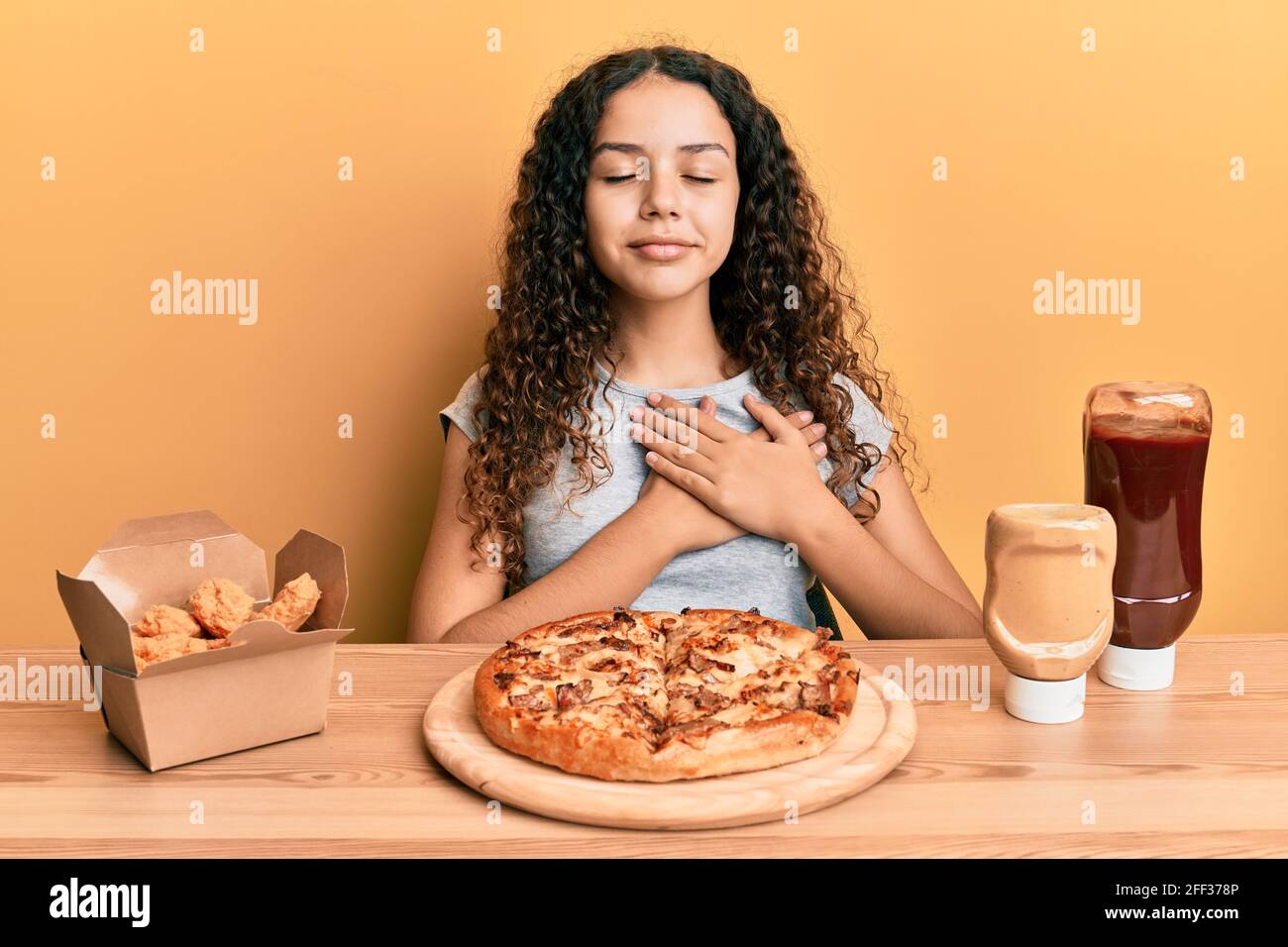 Teenager hispanic girl eating pizza and fried chicken smiling with ...