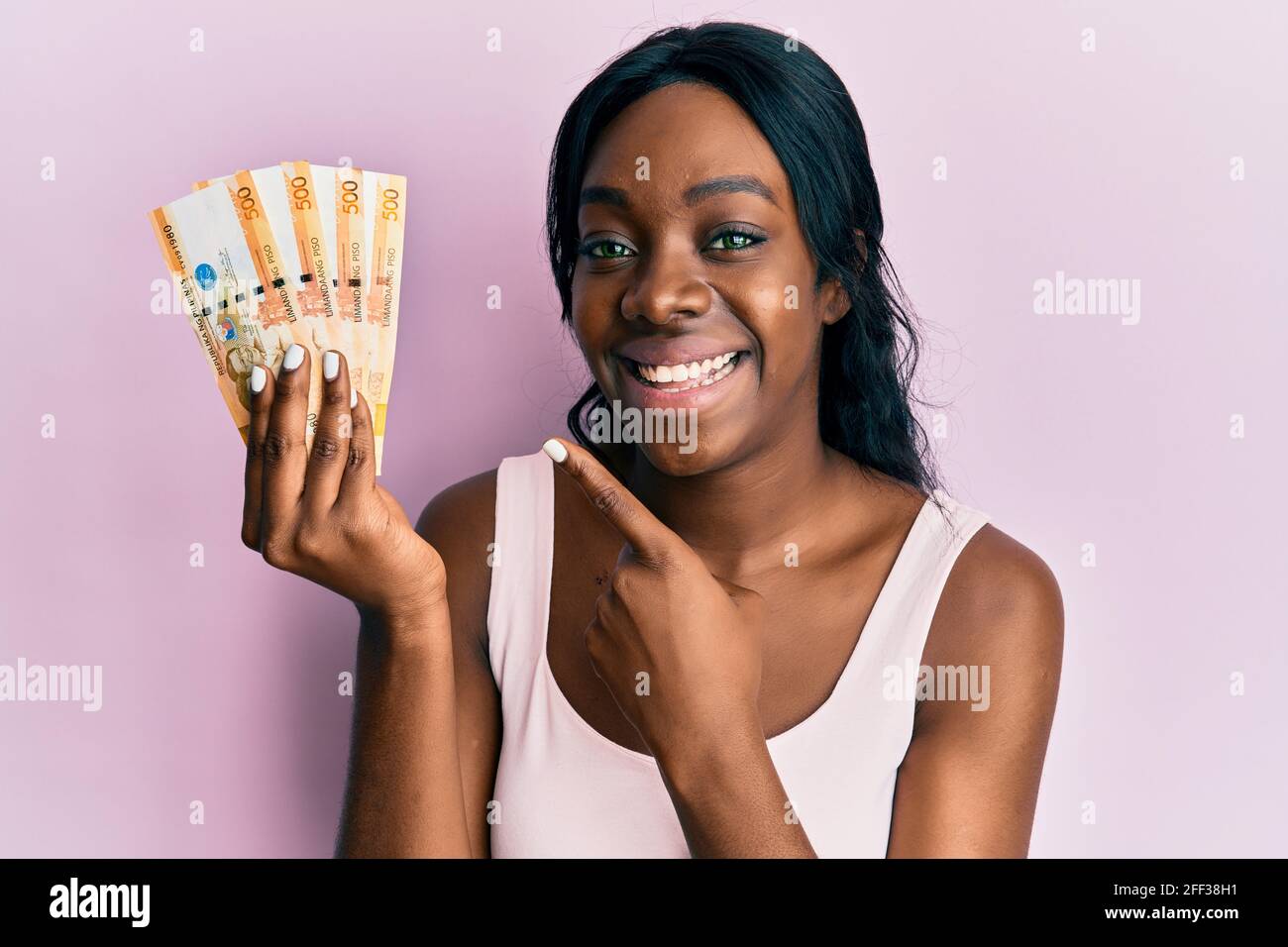 Young african american woman holding philippine peso banknotes smiling ...