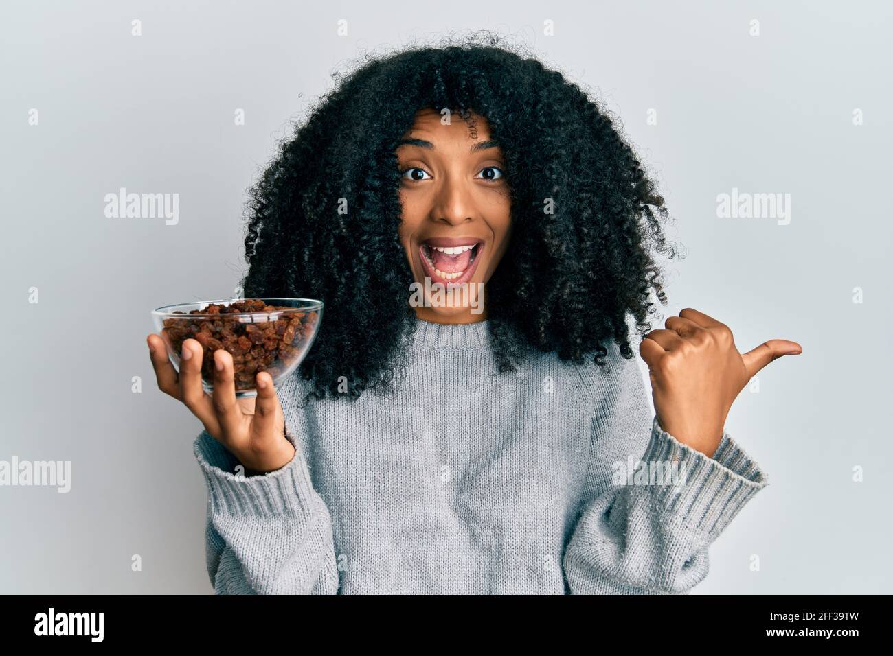 African american woman with afro hair holding raisins in bowl pointing ...