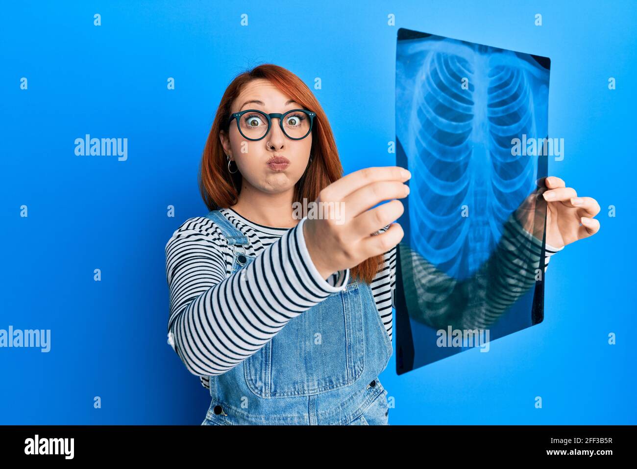 Beautiful redhead woman holding chest radiography puffing cheeks with ...