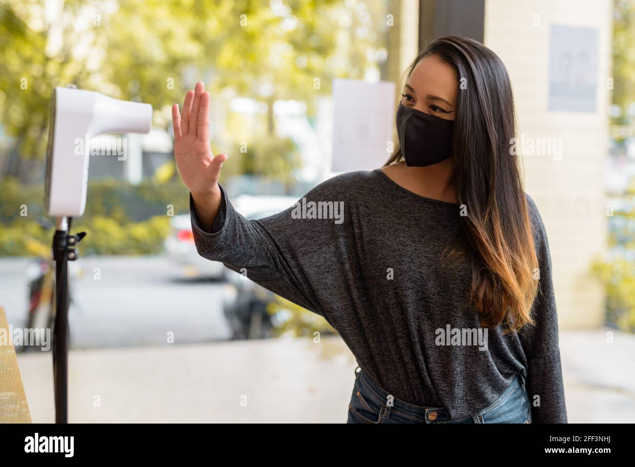 Woman wearing face mask and measuring body temperature while entering ...