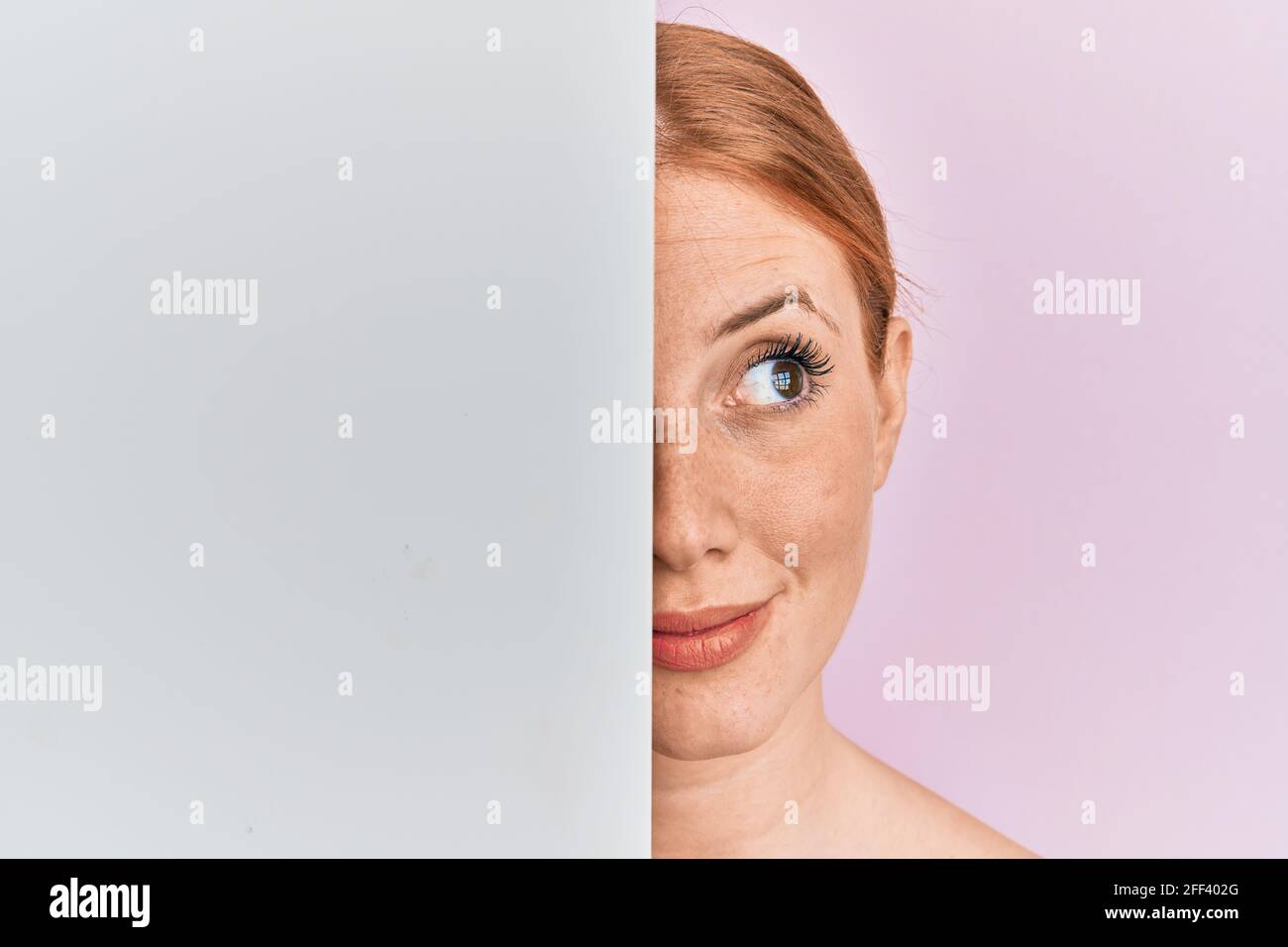 Young irish woman holding blank empty banner showing half face smiling ...