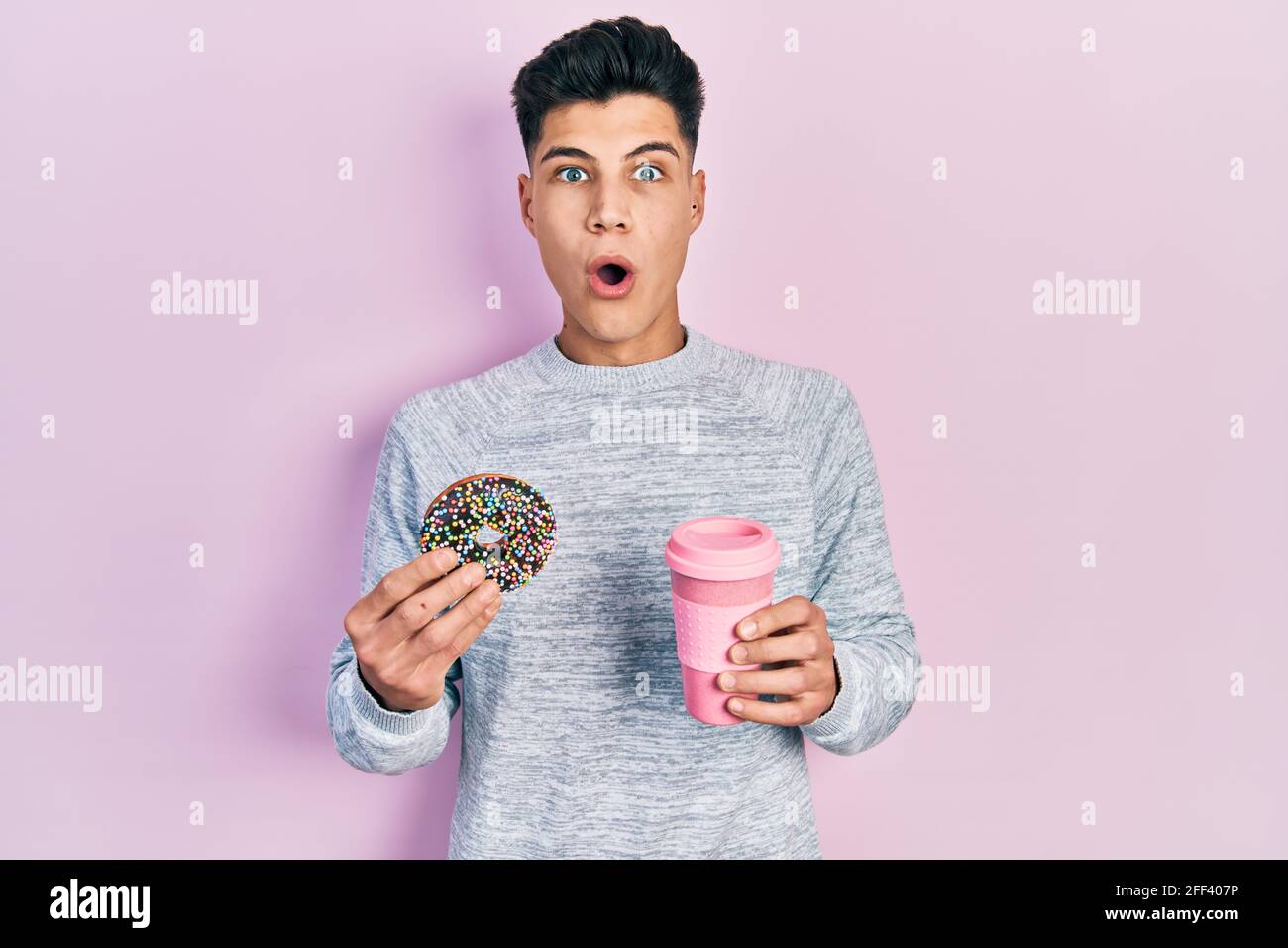 Young hispanic man eating doughnut and drinking coffee afraid and ...