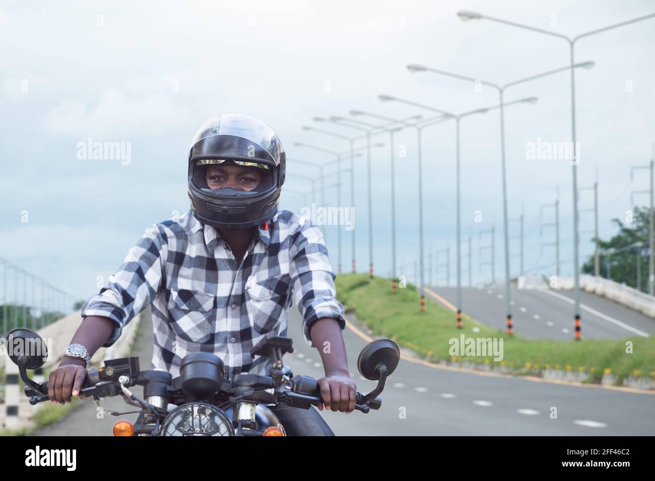 African biker in the helmet riding a motorcycle rides on highway road ...