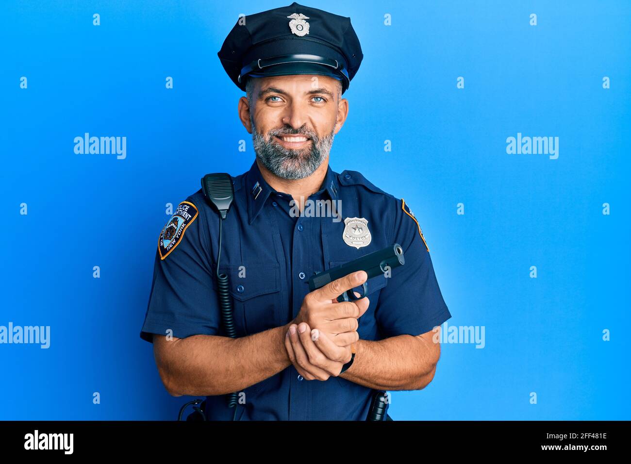 Middle age handsome man wearing police uniform holding gun smiling with ...