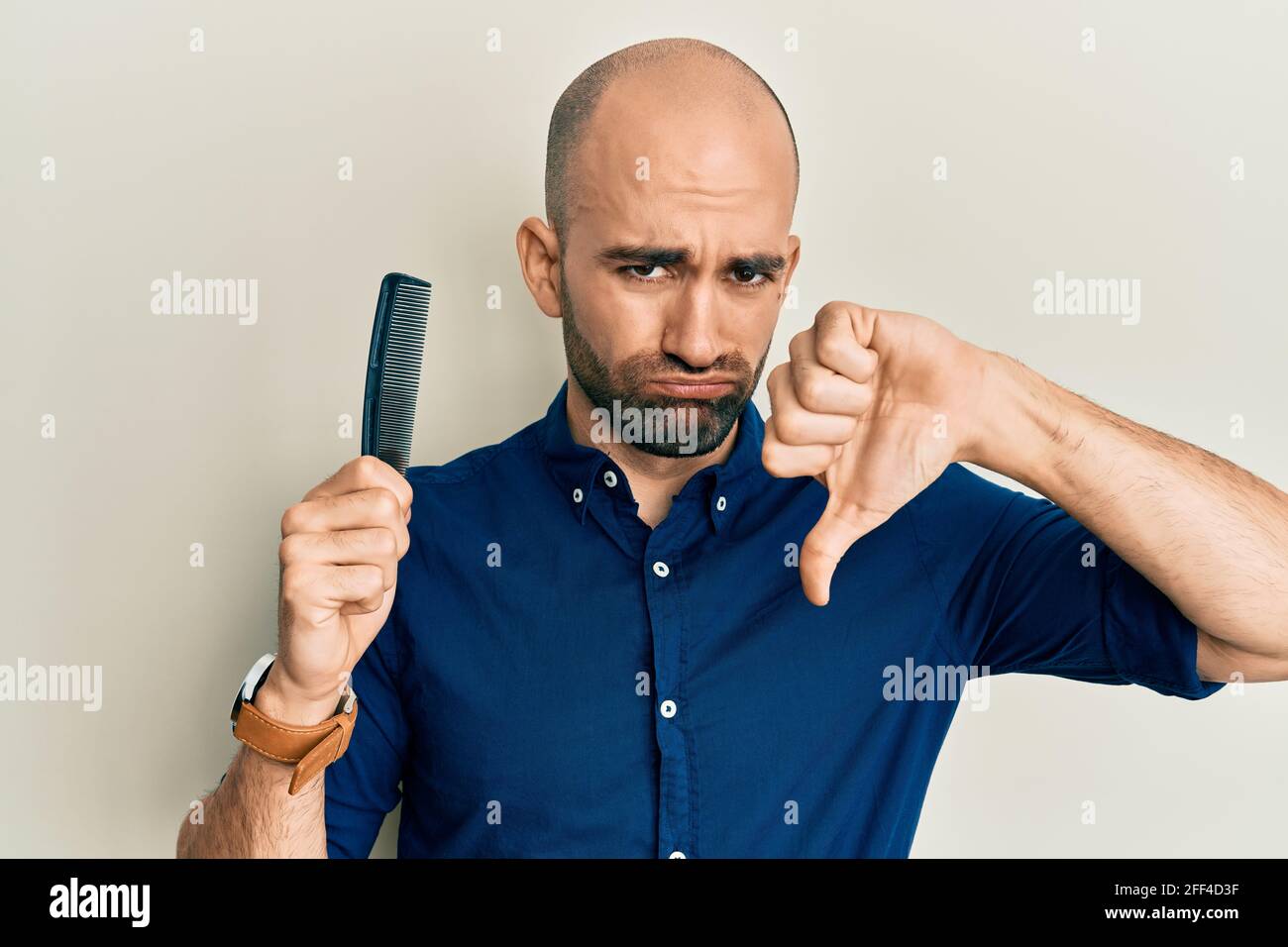 Young hispanic man holding comb loosing hair with angry face, negative ...