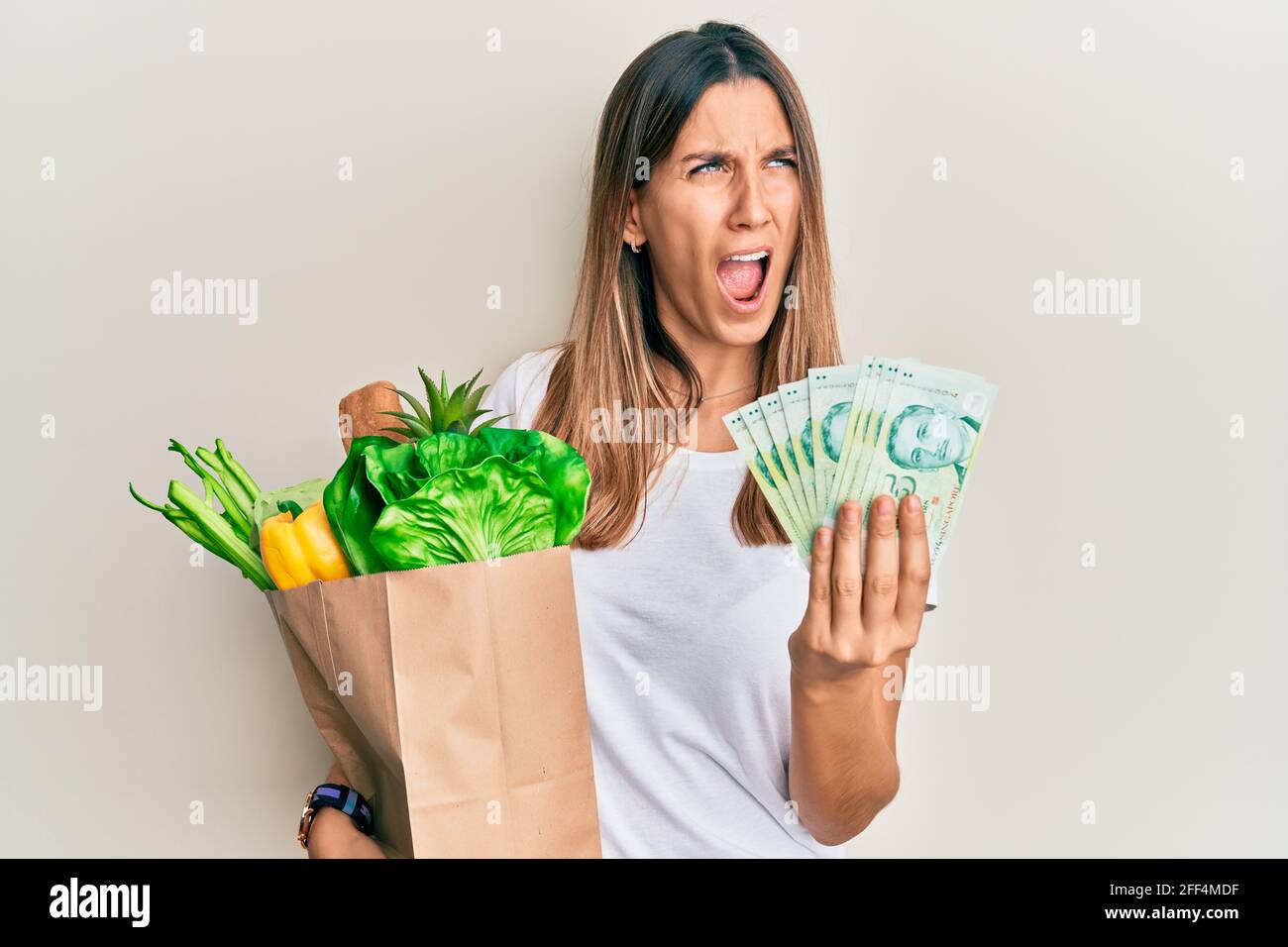Brunette young woman holding groceries and singapore dollars banknotes ...
