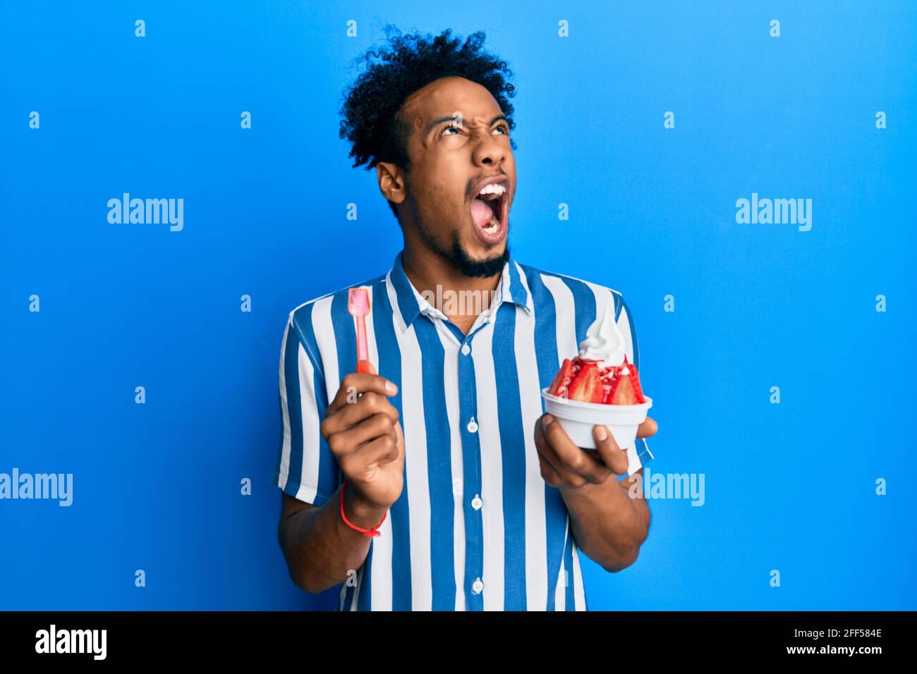 Young african american man with beard eating strawberry ice cream angry ...