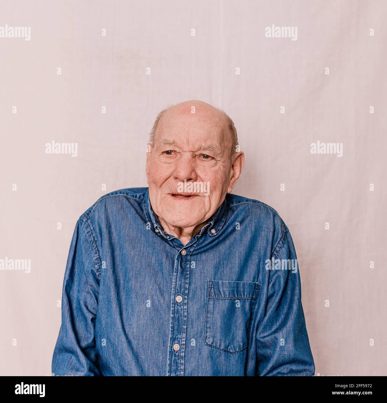 an old man with deep wrinkles on a light background. denim shirt ...