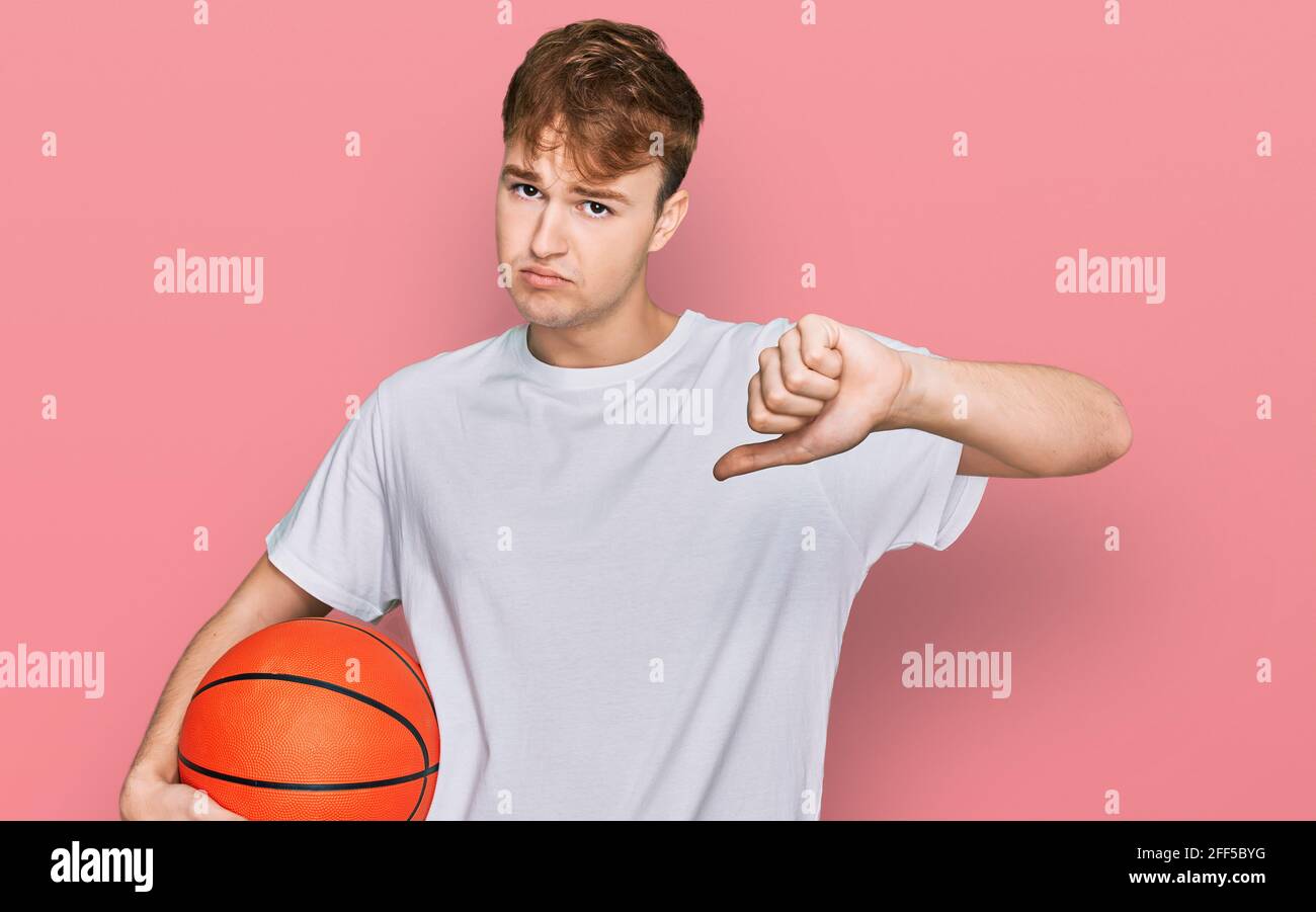 Young caucasian man holding basketball ball with angry face, negative ...