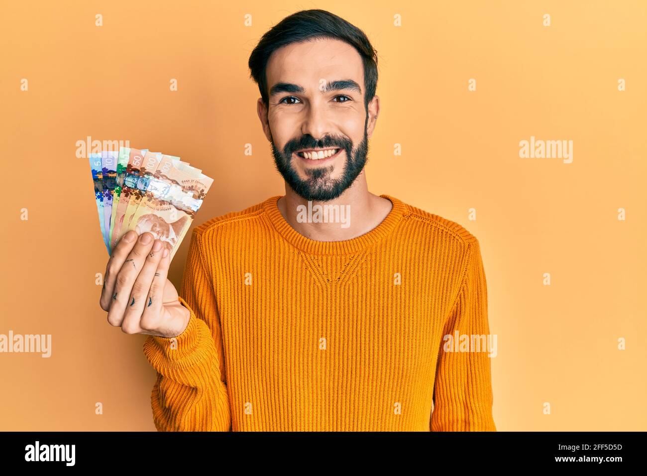 Young hispanic man holding canadian dollars looking positive and happy ...