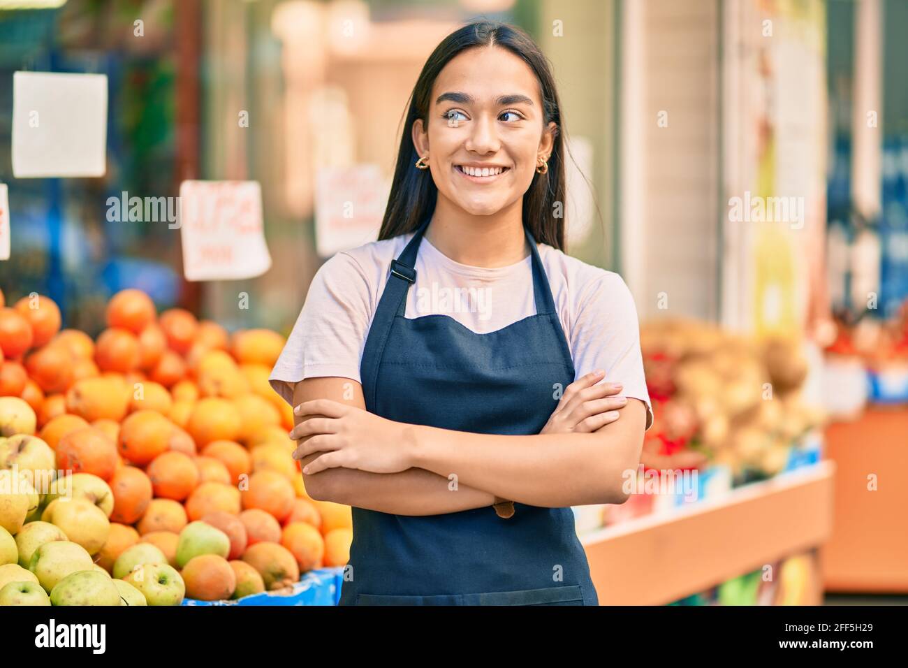 Young latin shopkeeper girl with arms crossed smiling happy at the ...