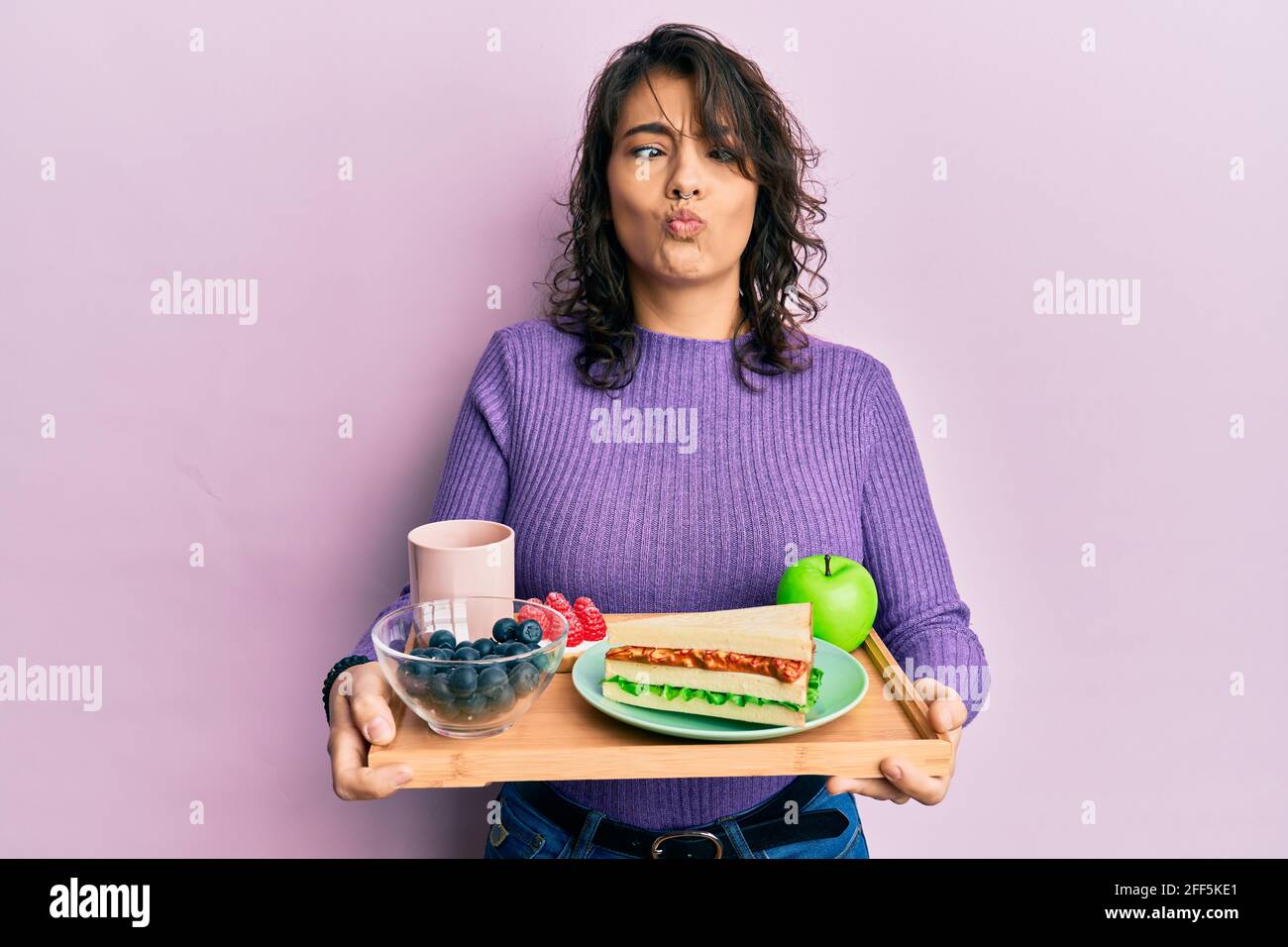 Young hispanic woman holding tray with breakfast food making fish face ...