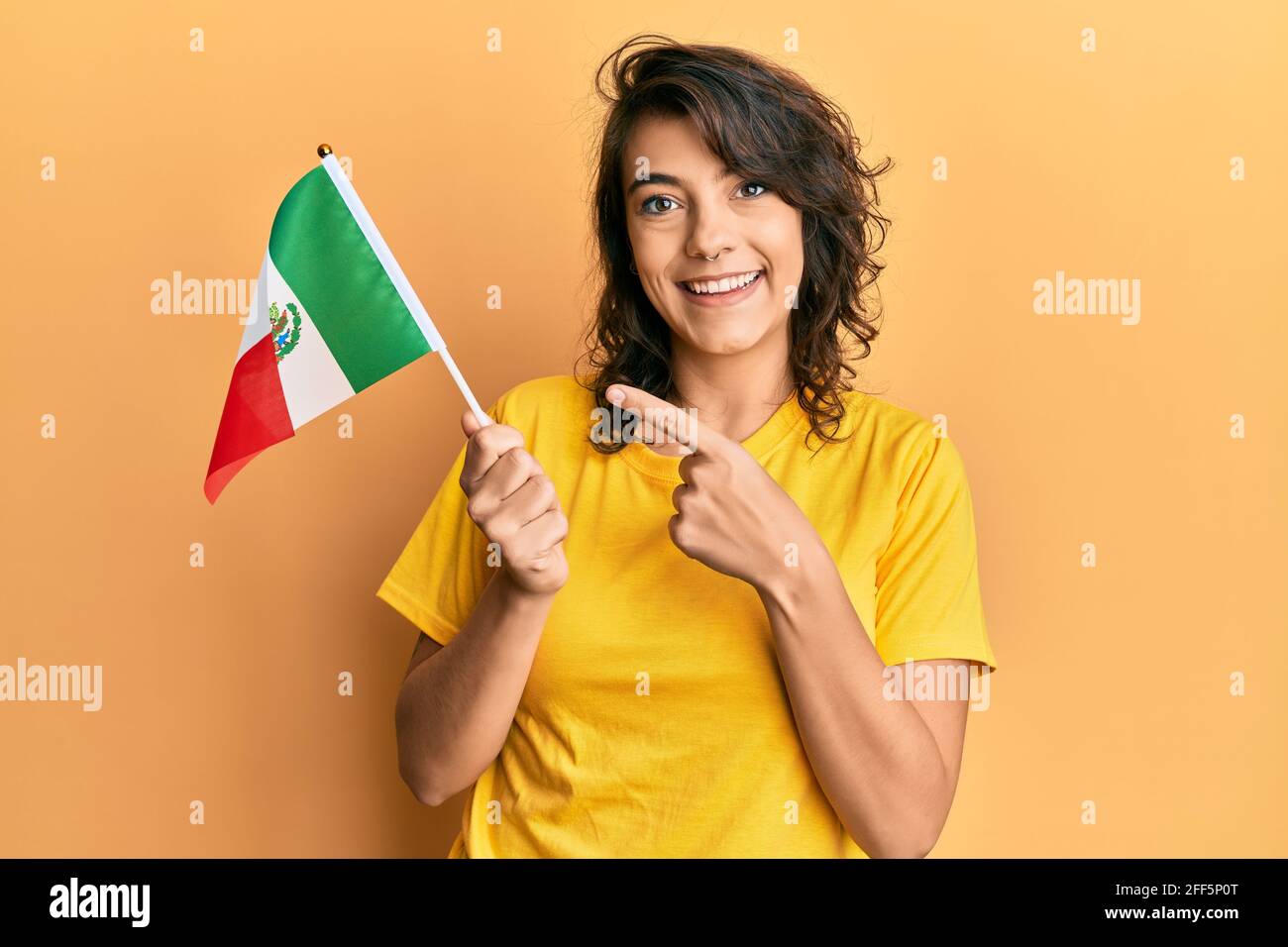 Young hispanic woman holding mexico flag smiling happy pointing with ...