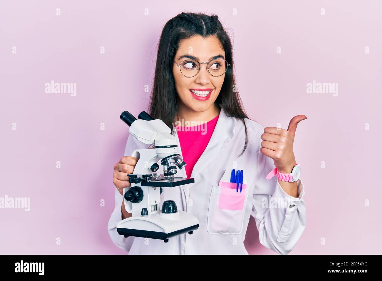 Young hispanic girl wearing scientist uniform holding microscope ...