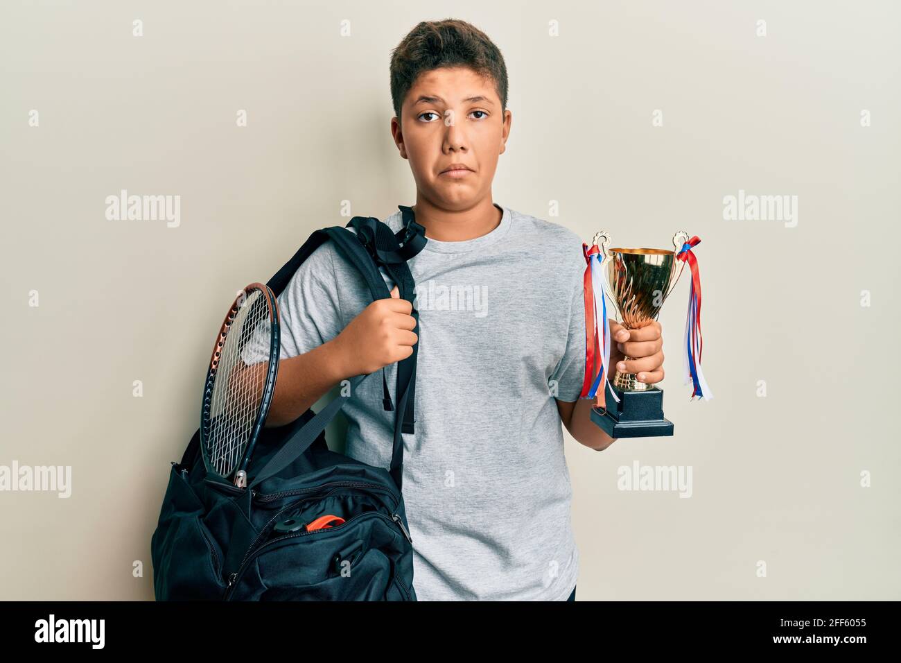 Teenager hispanic boy holding sport bag holding trophy depressed and ...