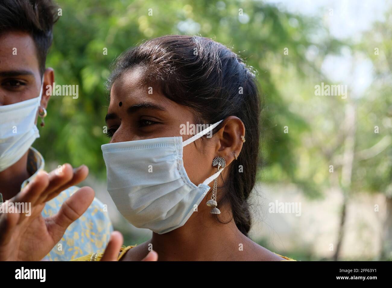 Young Indian female with a face mask explaining something with gestures ...