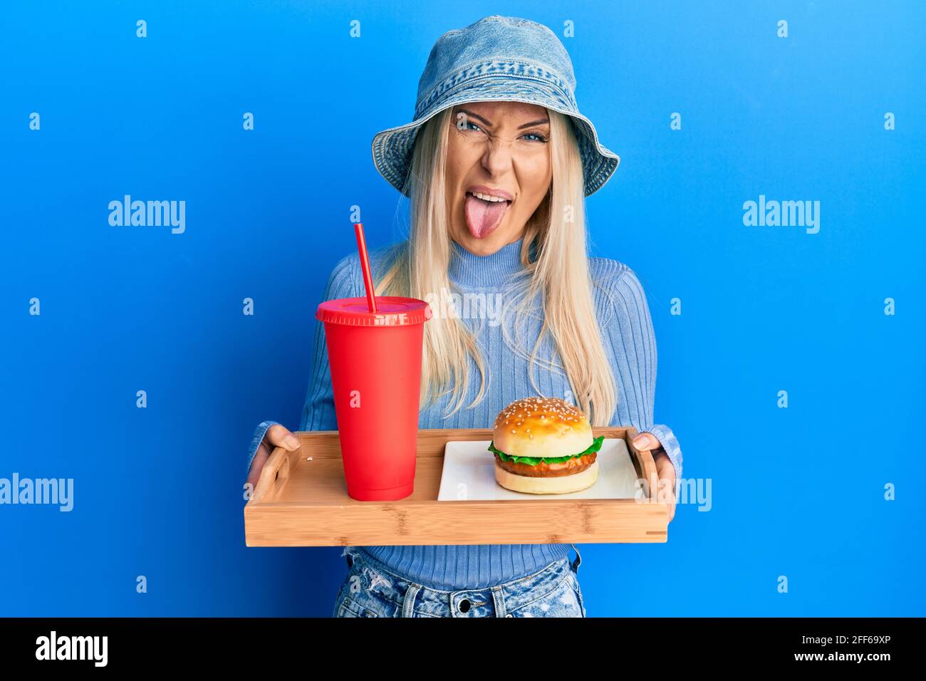 Young blonde woman eating a tasty classic burger and soda sticking ...