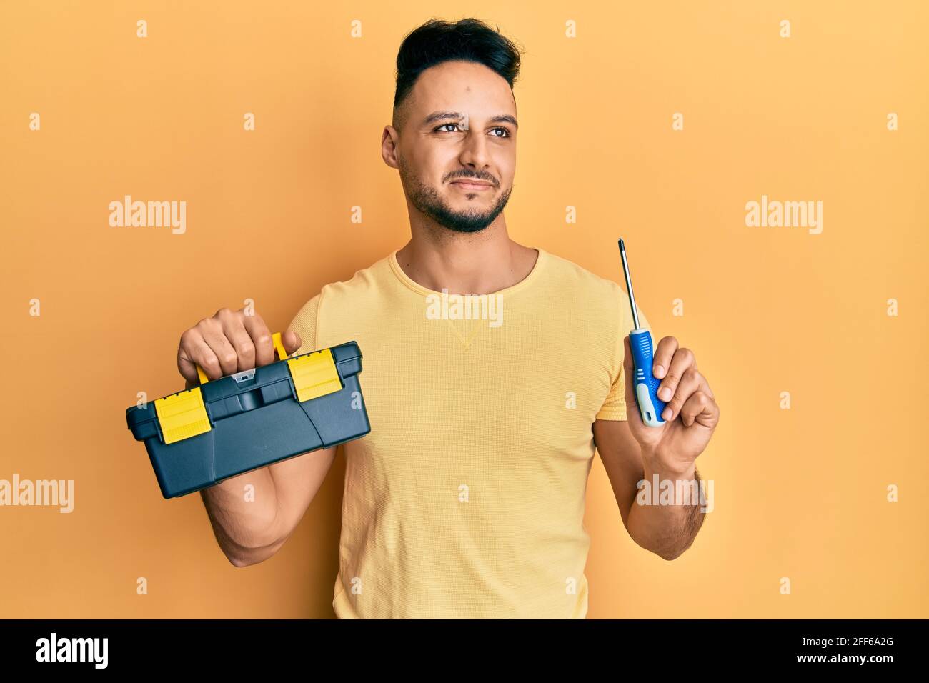 Young arab man holding toolbox and screwdriver smiling looking to the ...