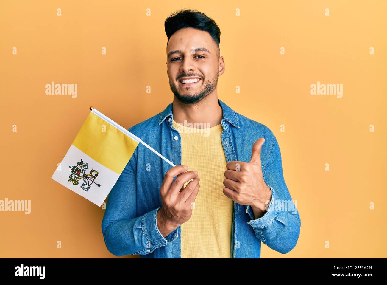 Young arab man holding vatican city flag smiling happy and positive ...