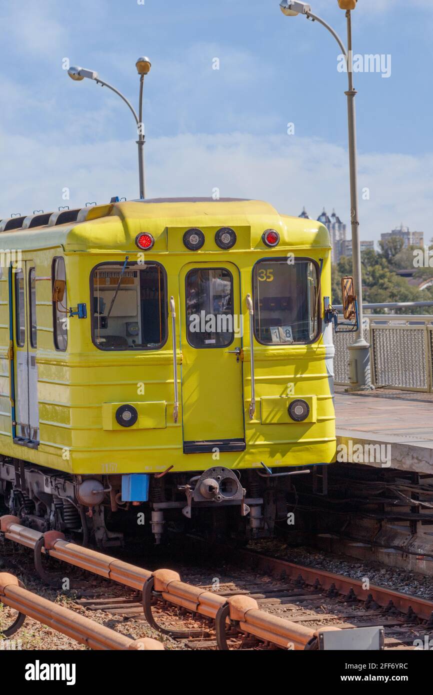 A bright yellow subway train carriage on the platform of a metro bridge ...