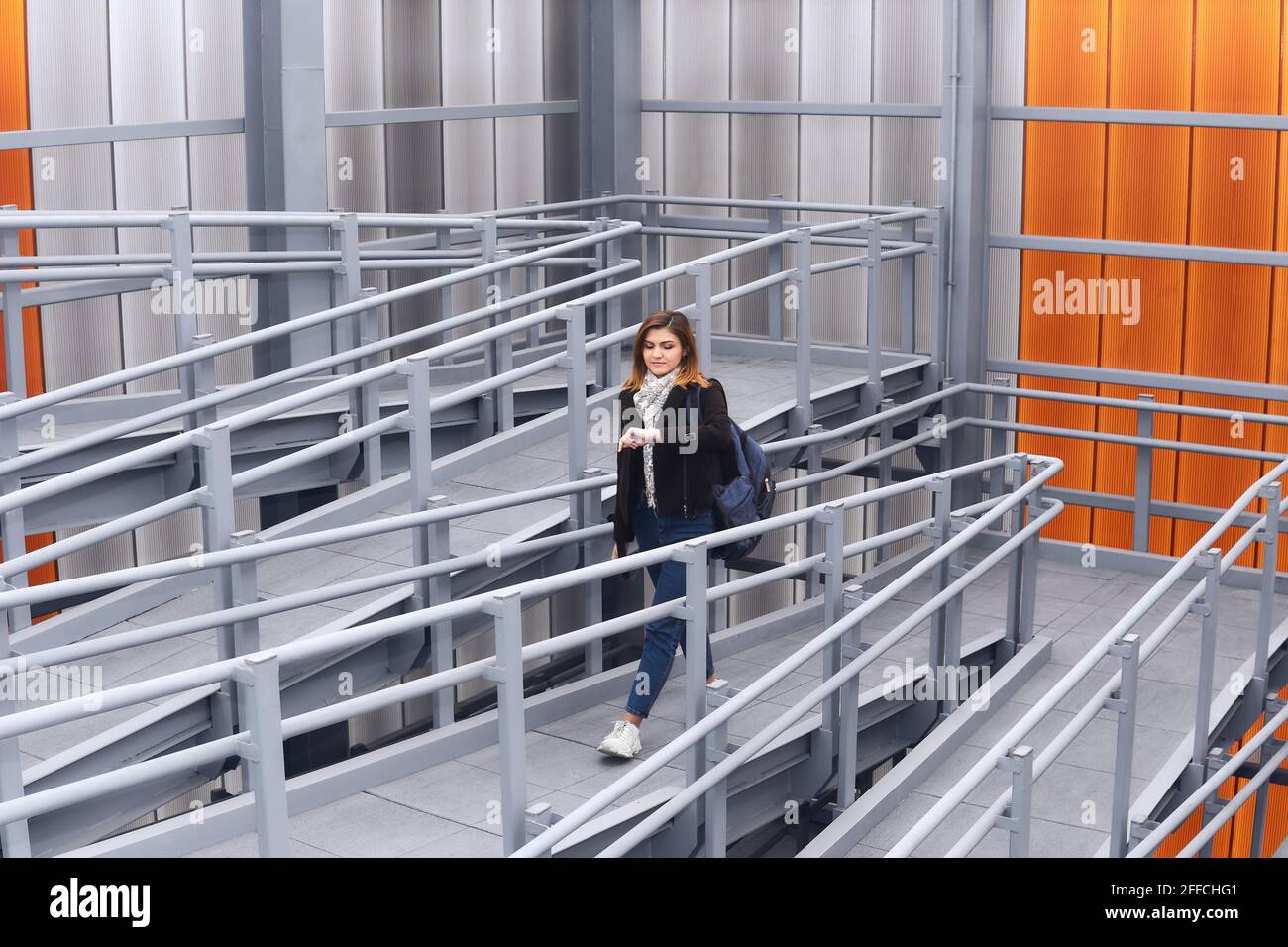 young woman looks at her watch as she climbs the zigzag ramp of a ...