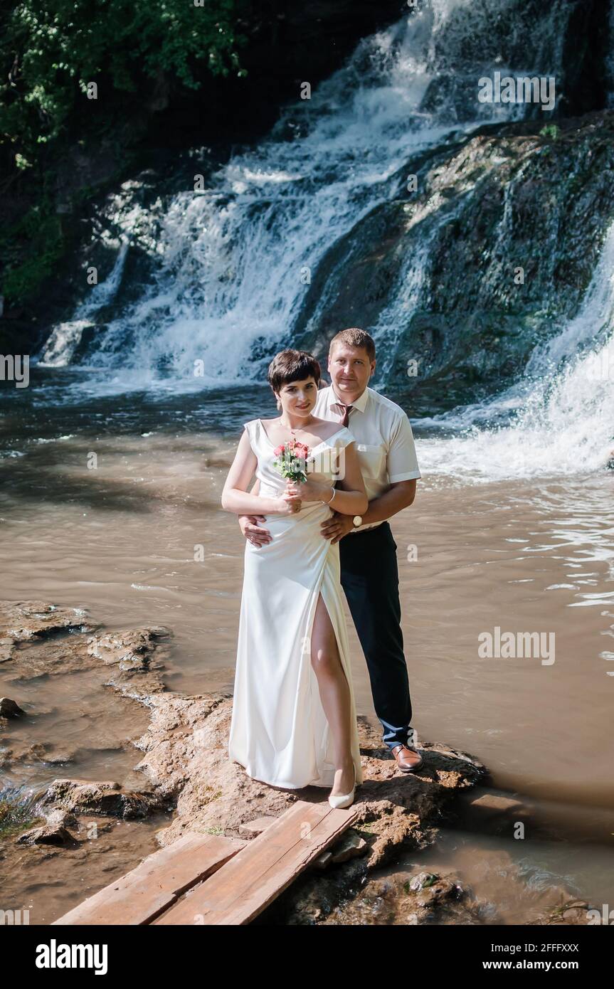 The bride and groom stand against the background of a waterfall Stock ...