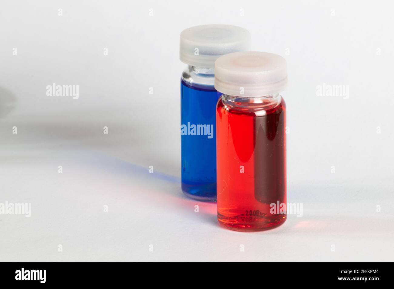 Two small transparent containers with red and blue liquid on white ...