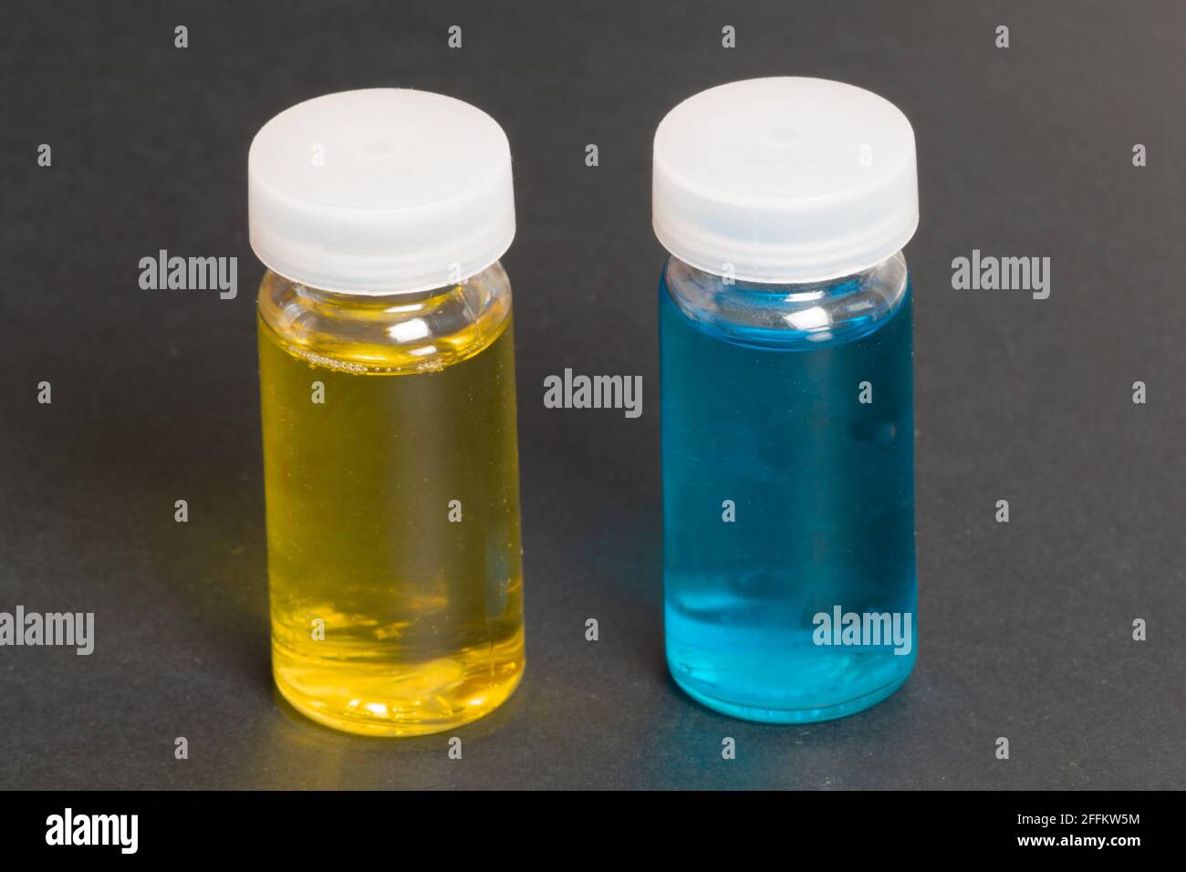transparent containers with yellow and blue liquid on black background ...