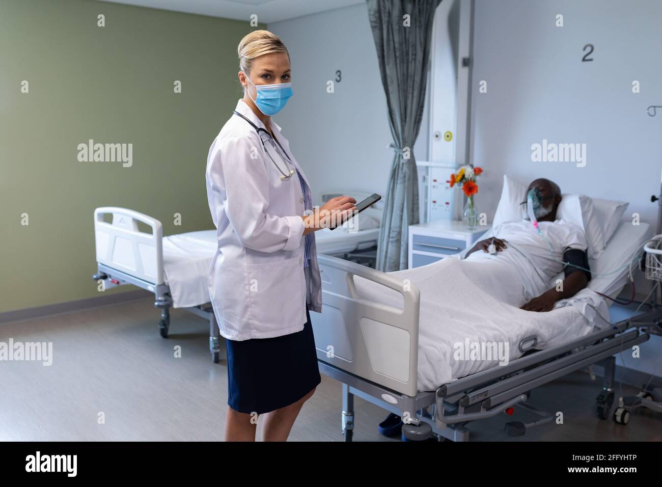 Caucasian female doctor wearing face mask holding tablet looking to ...