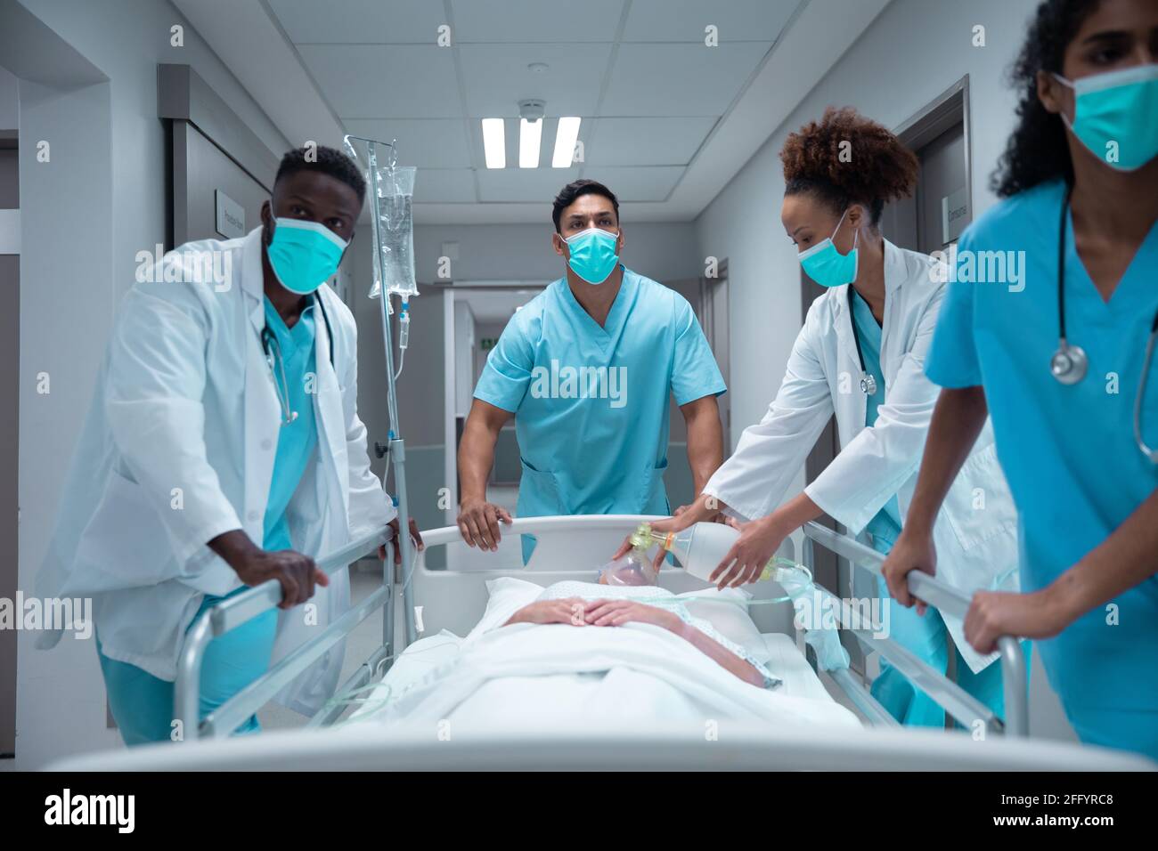 Mixed race doctors wearing face masks transporting patient in hospital ...