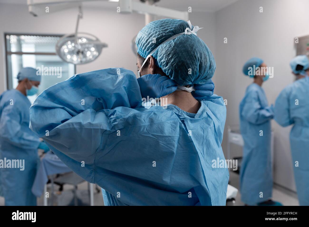 Mixed race doctor putting on face mask and surgical overalls standing ...